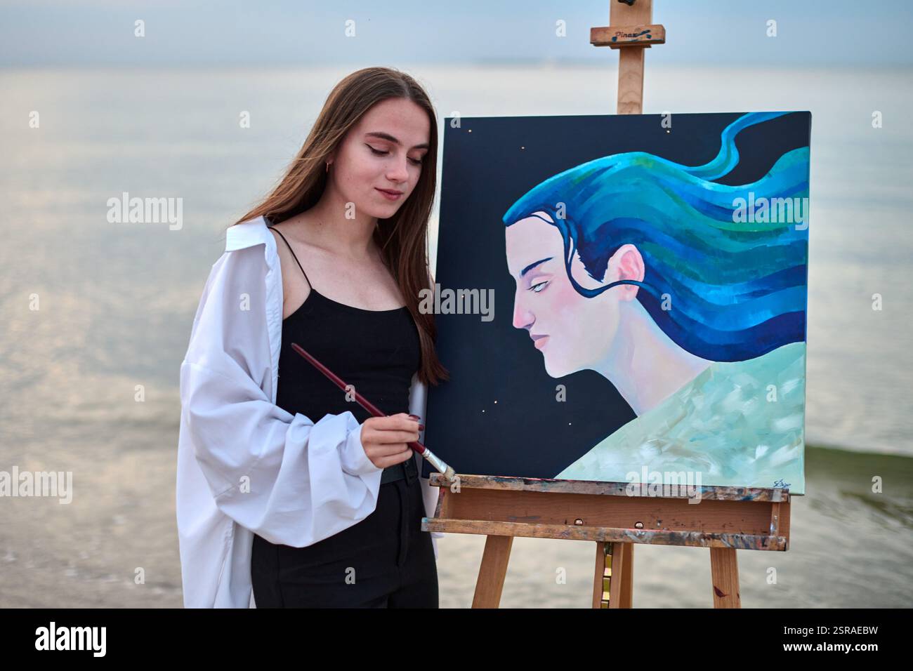 Young female painter stands by sea, proudly displaying her vivid ...