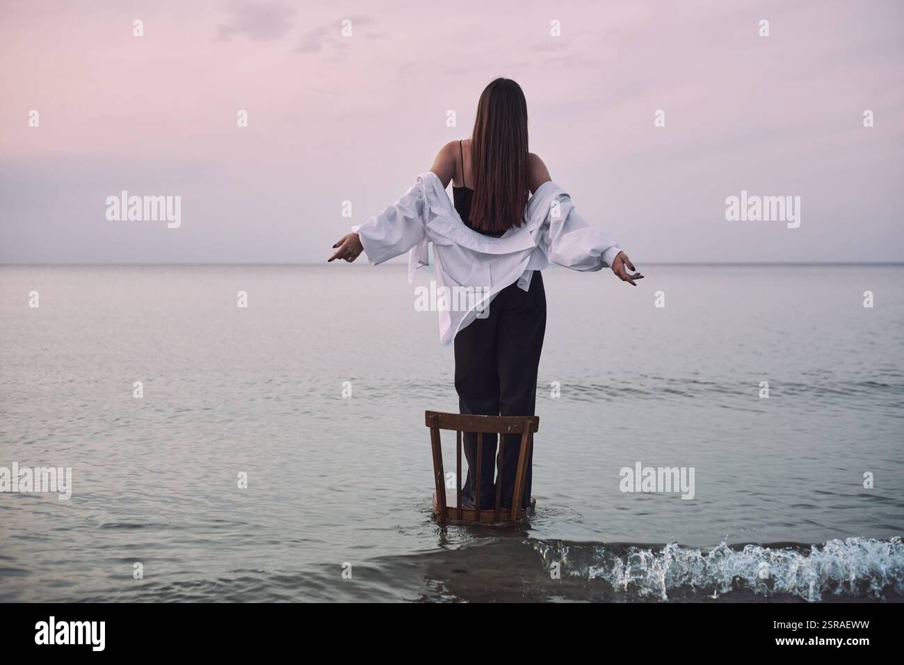 Young woman stands gracefully on chair in shallow sea water, arms ...