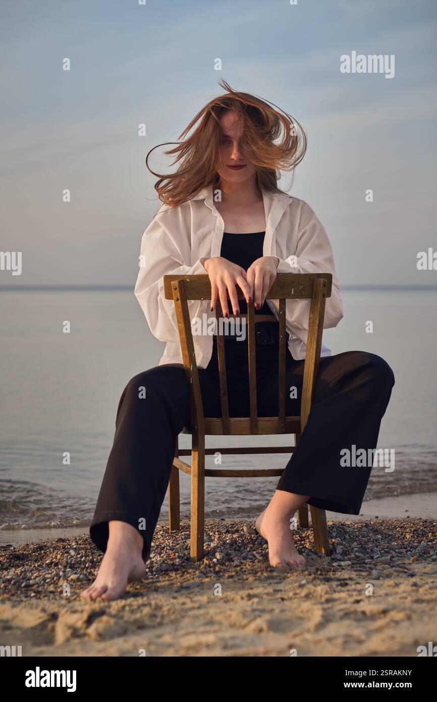 Young woman sits on chair facing calm sea, symbolizing solitude and ...