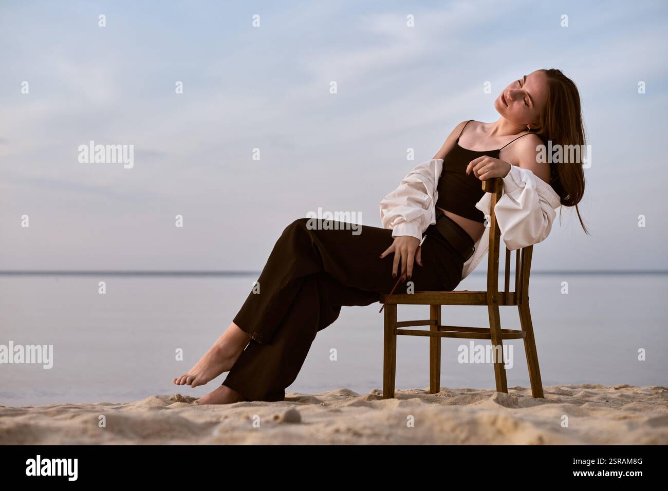 Young female painter sits thoughtfully on chair by tranquil beach ...