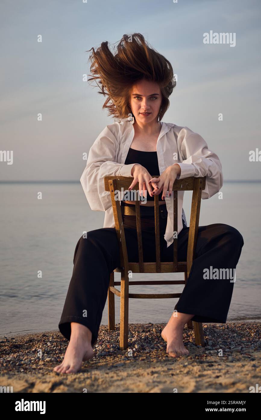 Young woman sits on chair facing calm sea, symbolizing solitude and ...