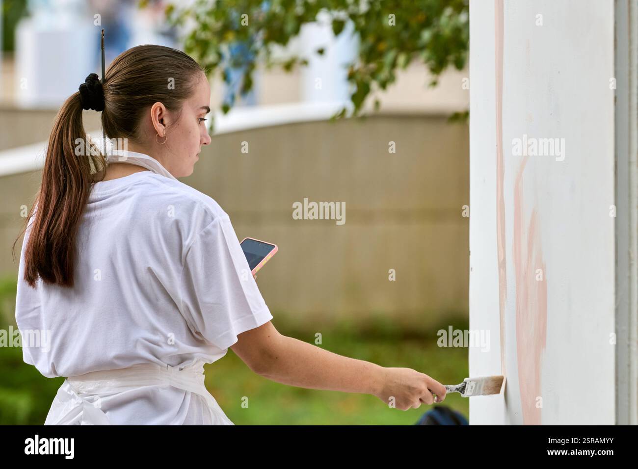 Young adult caucasian female painting large wall with brush in outdoor ...