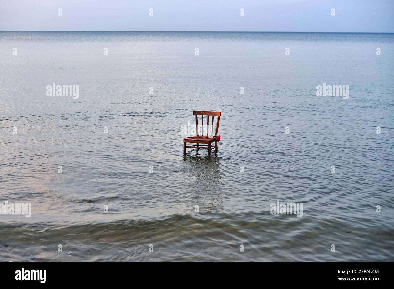 Wooden chair stands in calm, vast ocean, symbolizing solitude and ...