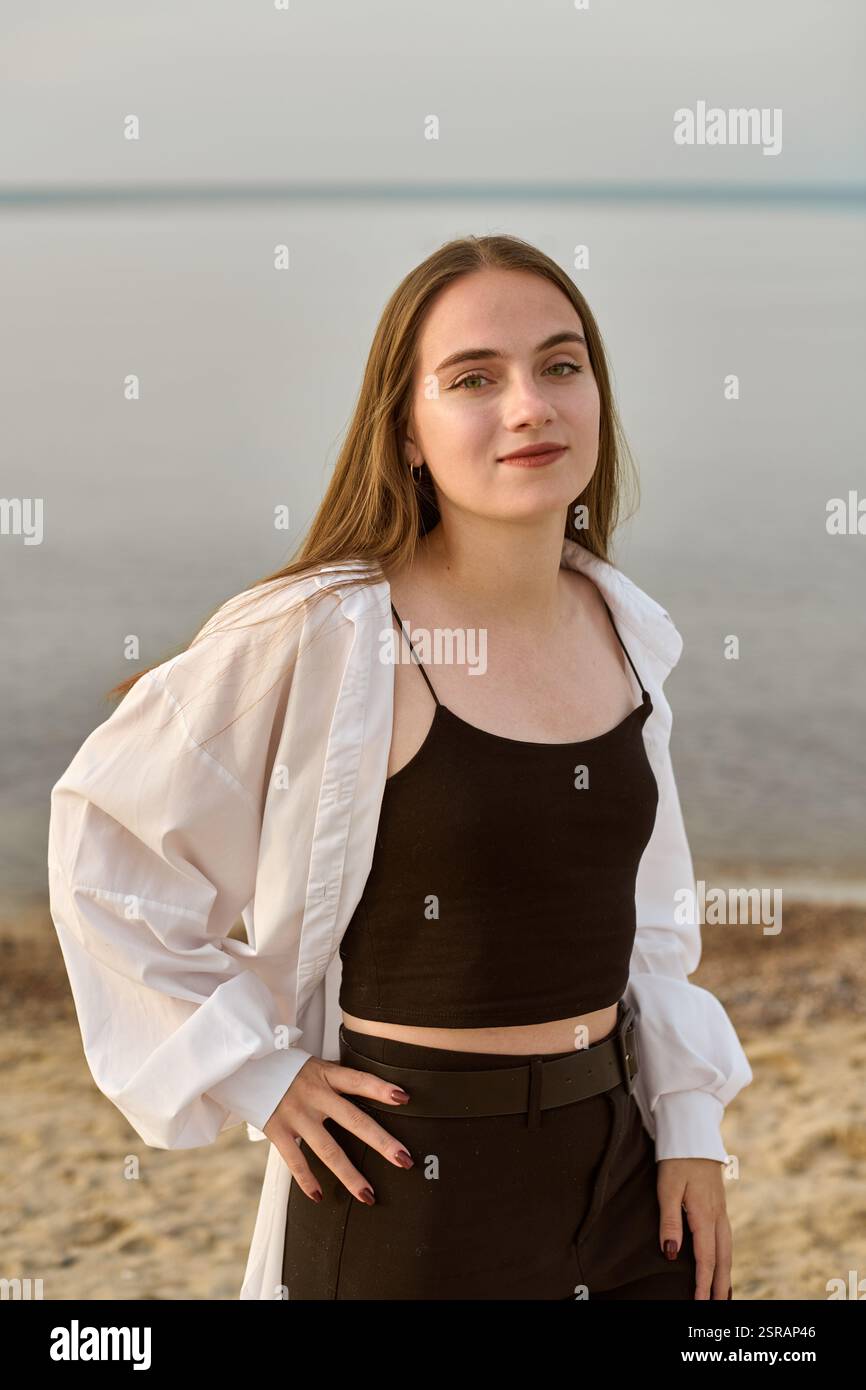 Young woman stands confidently by tranquil seaside. Her relaxed pose ...