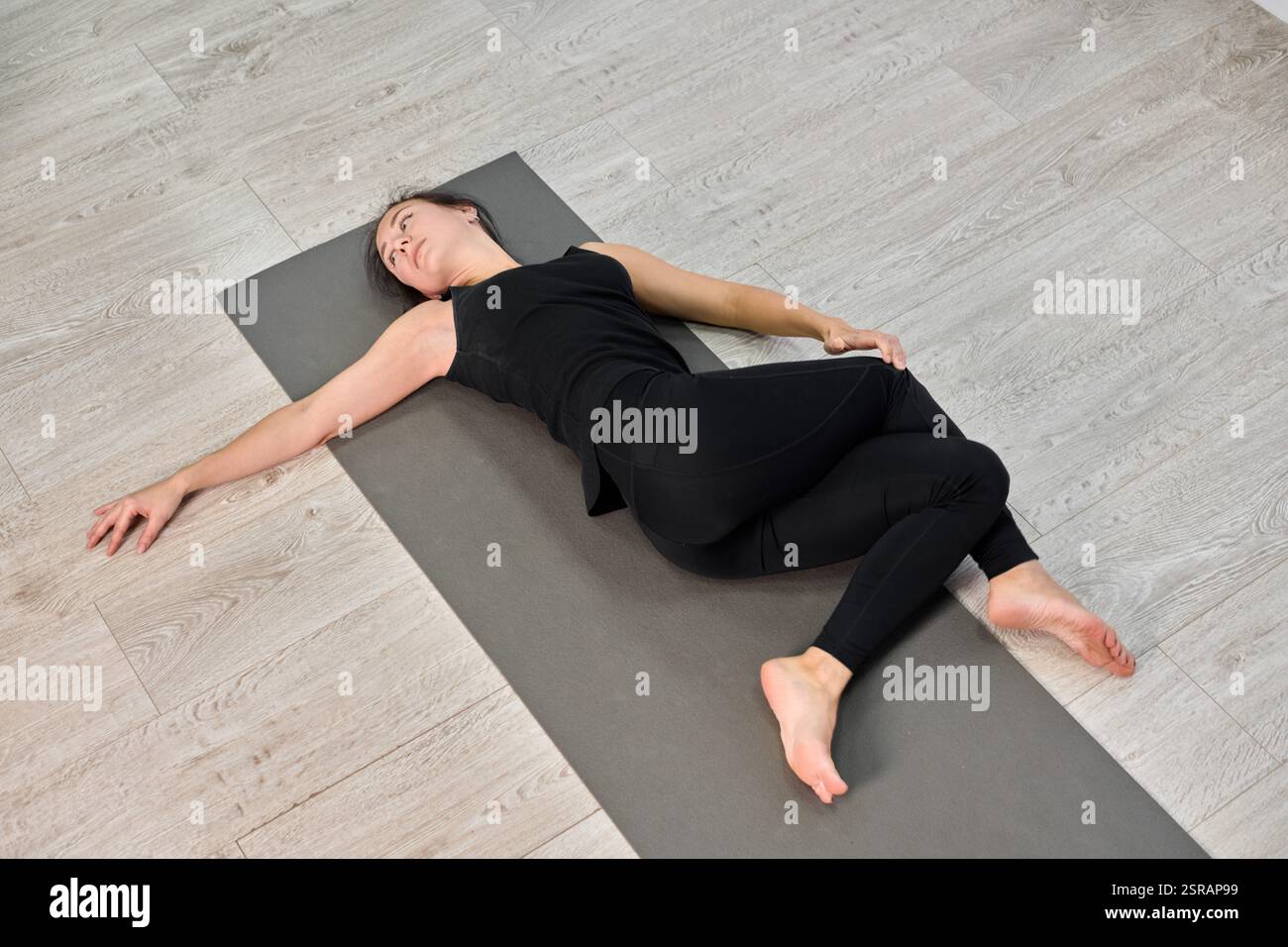 Young asian woman in black activewear demonstrates supine twist yoga ...