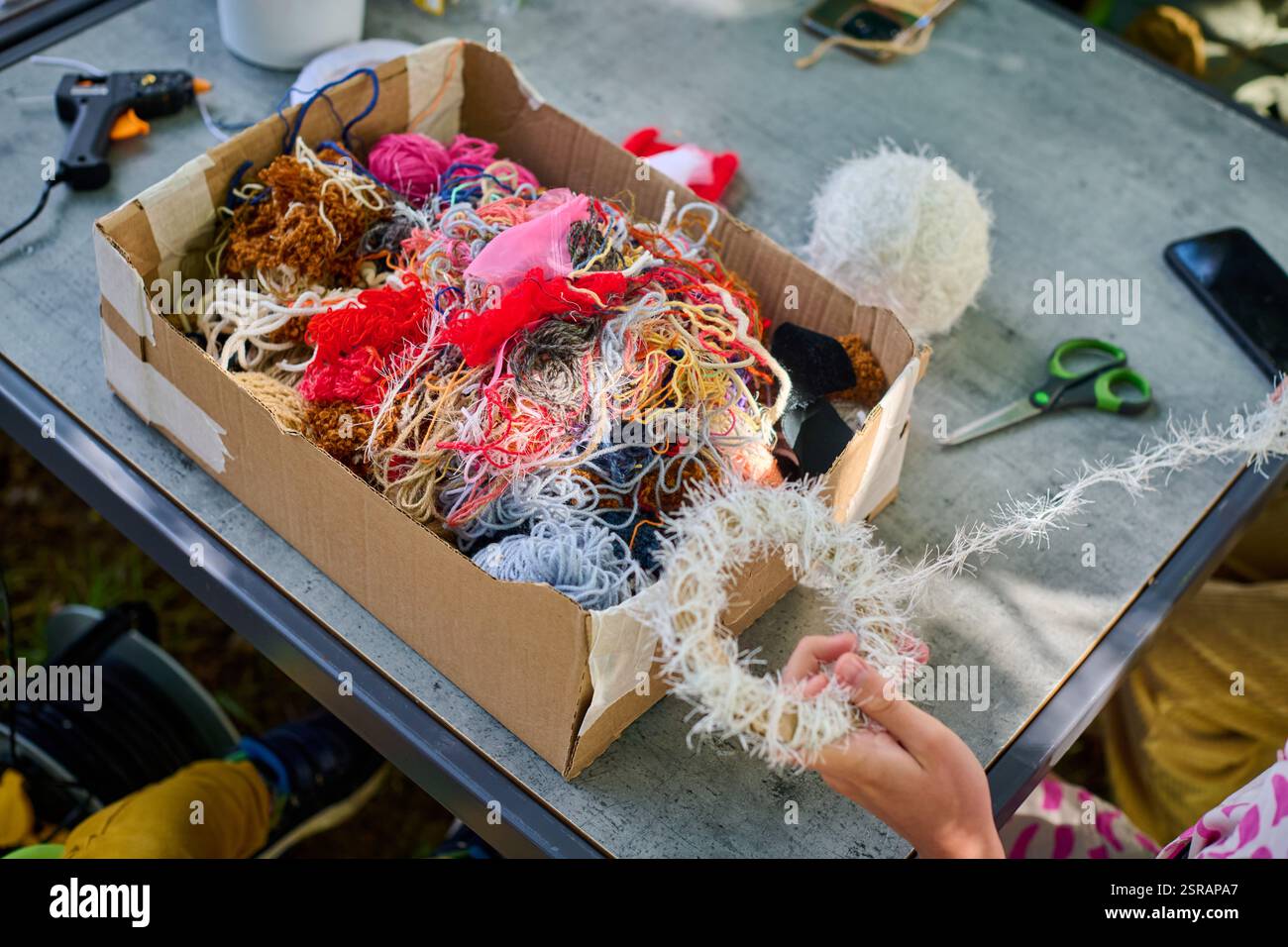 Child creating with colorful yarn at outdoor table. Box of assorted ...