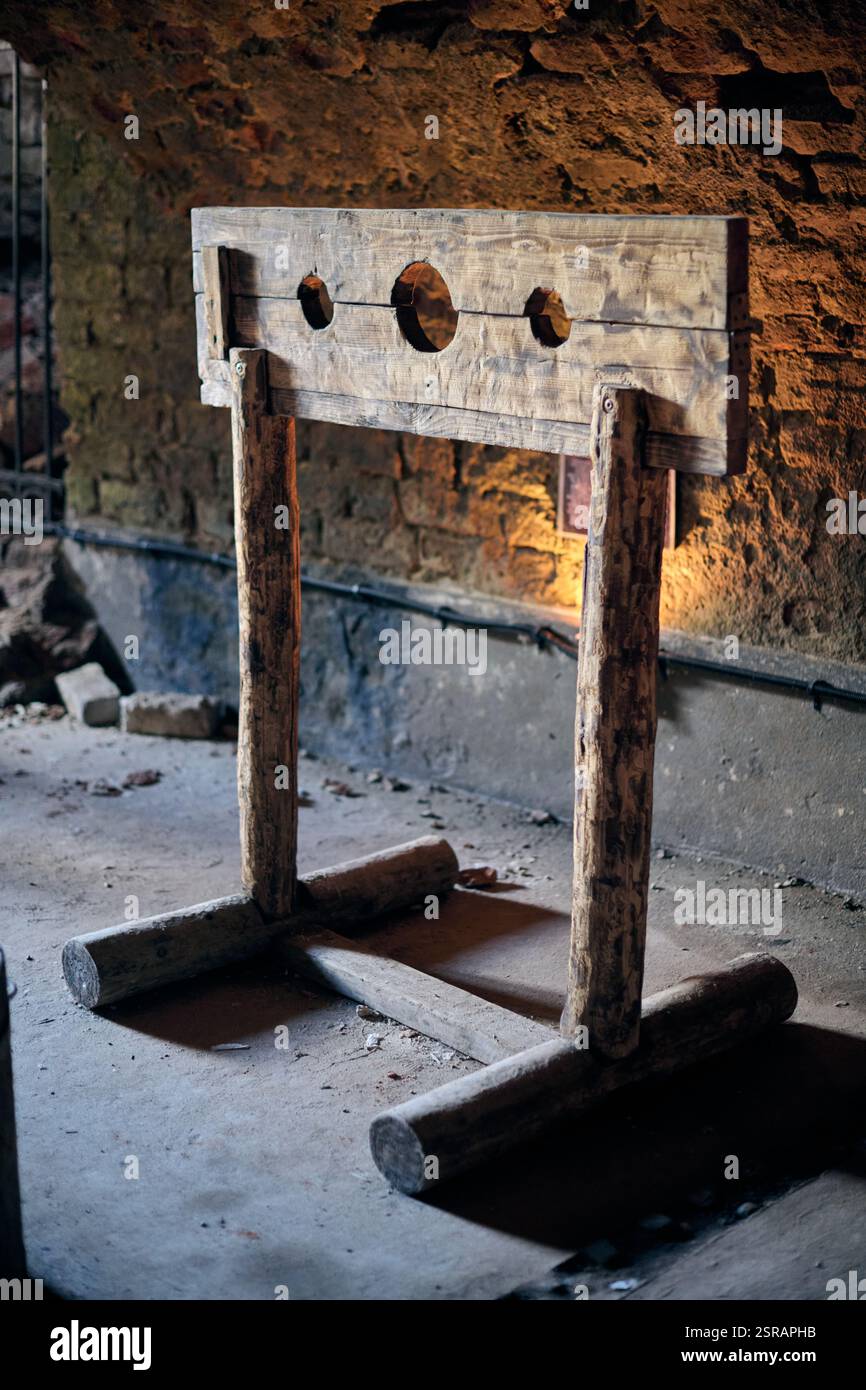 Pillory in dimly lit museum dungeon, shadows flickering across cold ...