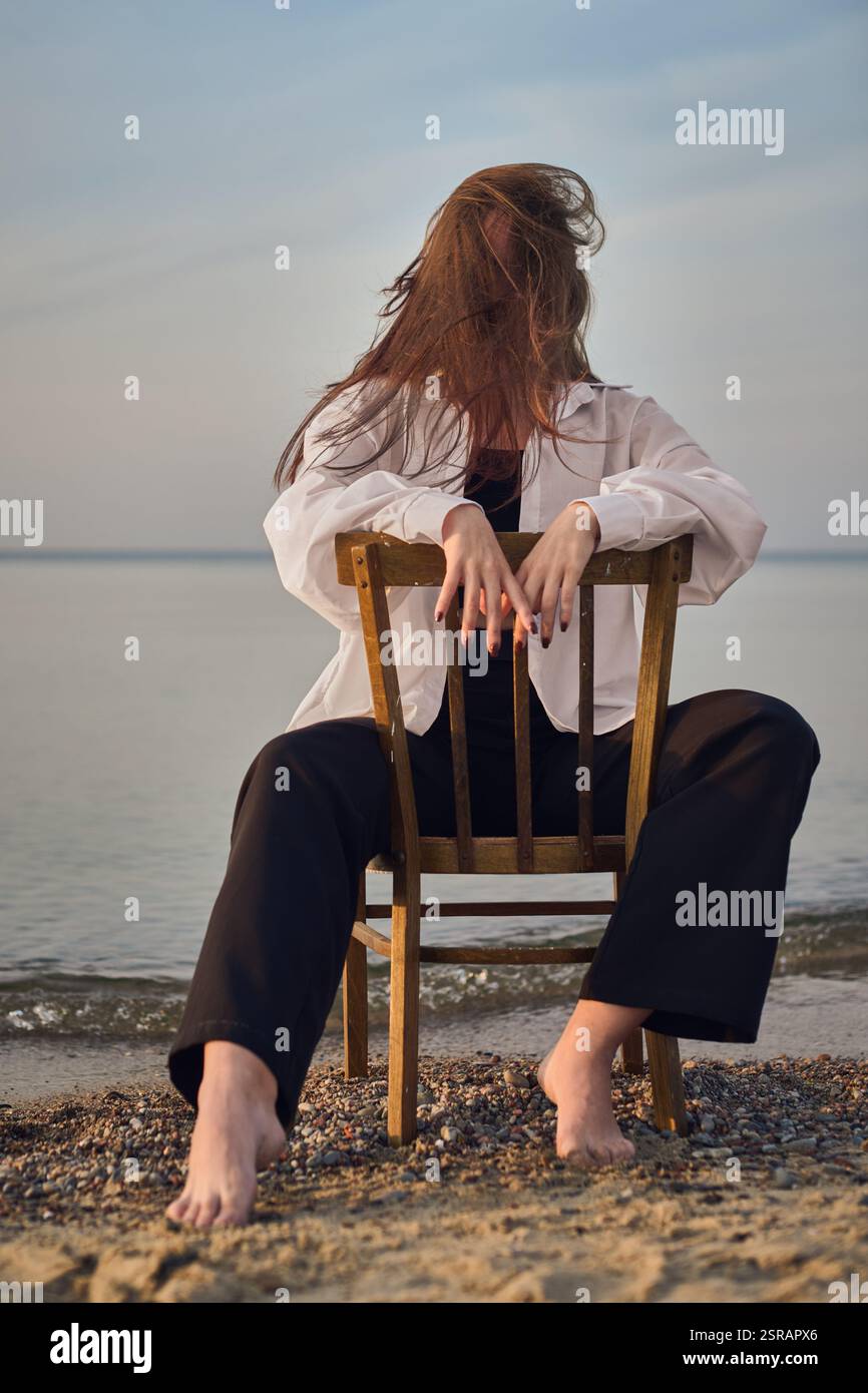 Young woman sits on chair facing calm sea, symbolizing solitude and ...