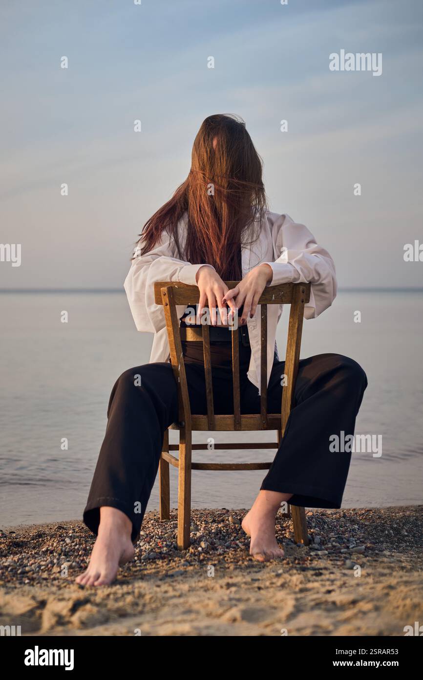 Young woman sits on chair facing calm sea, symbolizing solitude and ...