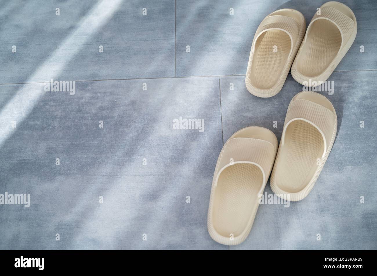 two pairs of beige rubber slippers stand on a gray granite floor Stock ...
