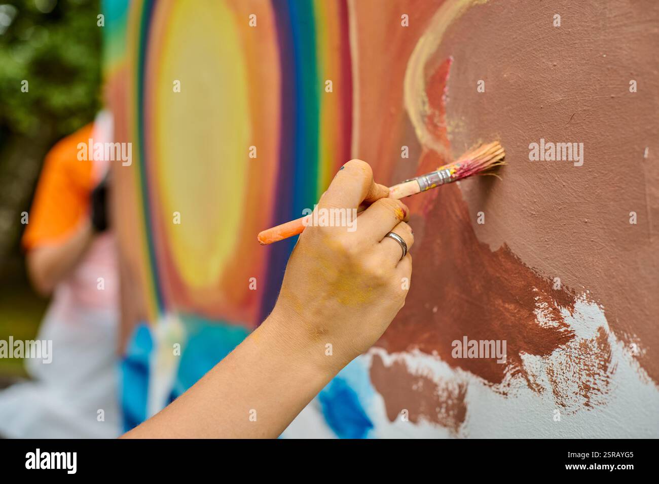 Young caucasian female uses paintbrush to create vibrant mural on ...