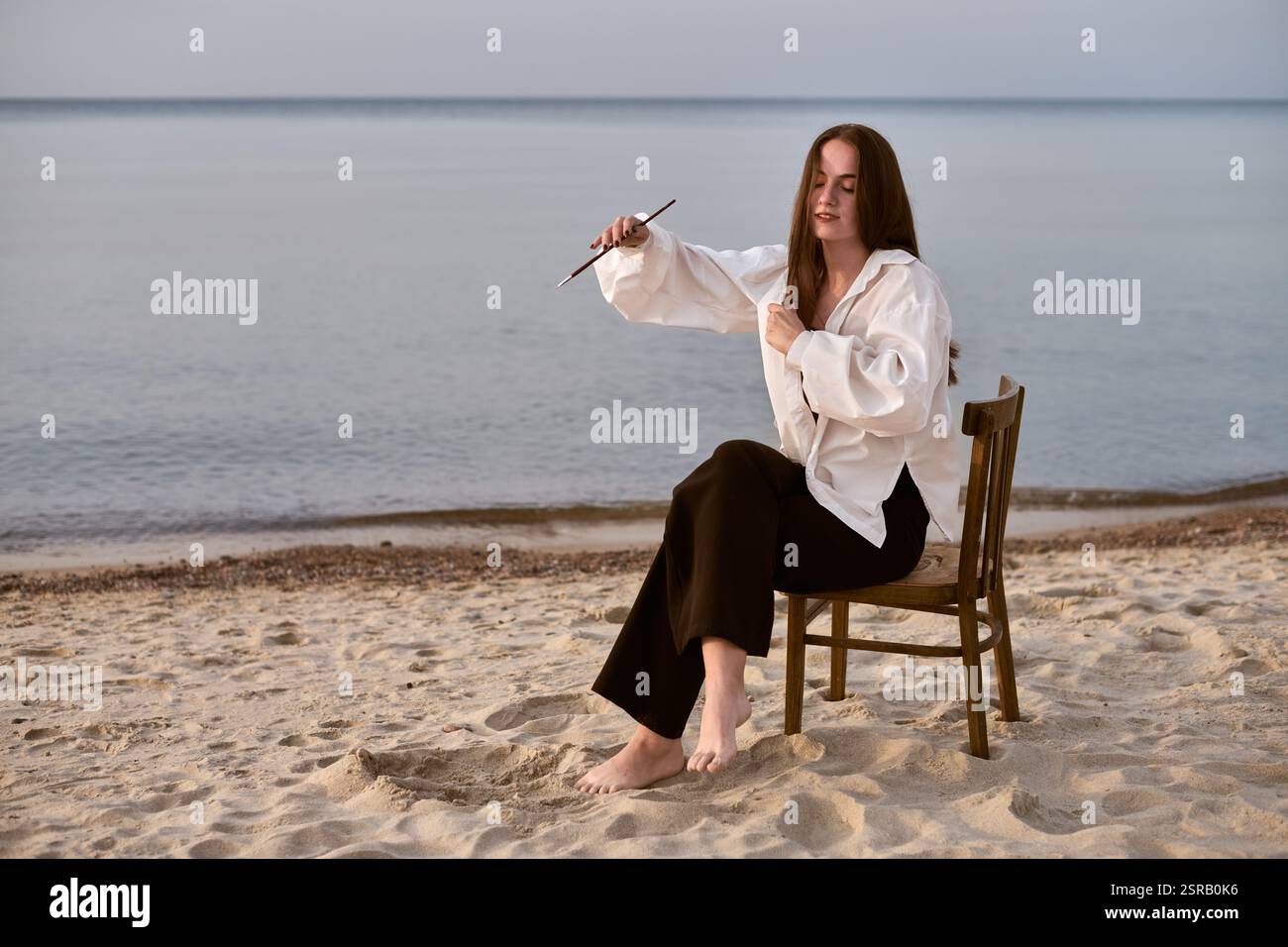 Young female artist enjoys quiet reflection on beach, holding ...