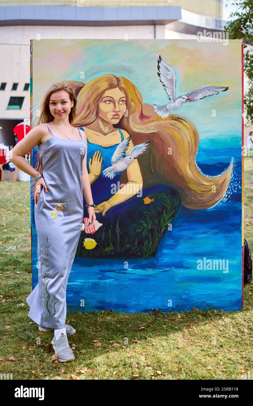 Young female artist with brown hair stands proudly by colorful mermaid ...