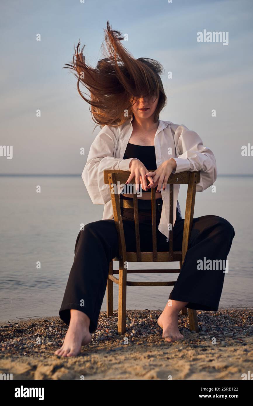 Young woman sits on chair facing calm sea, symbolizing solitude and ...