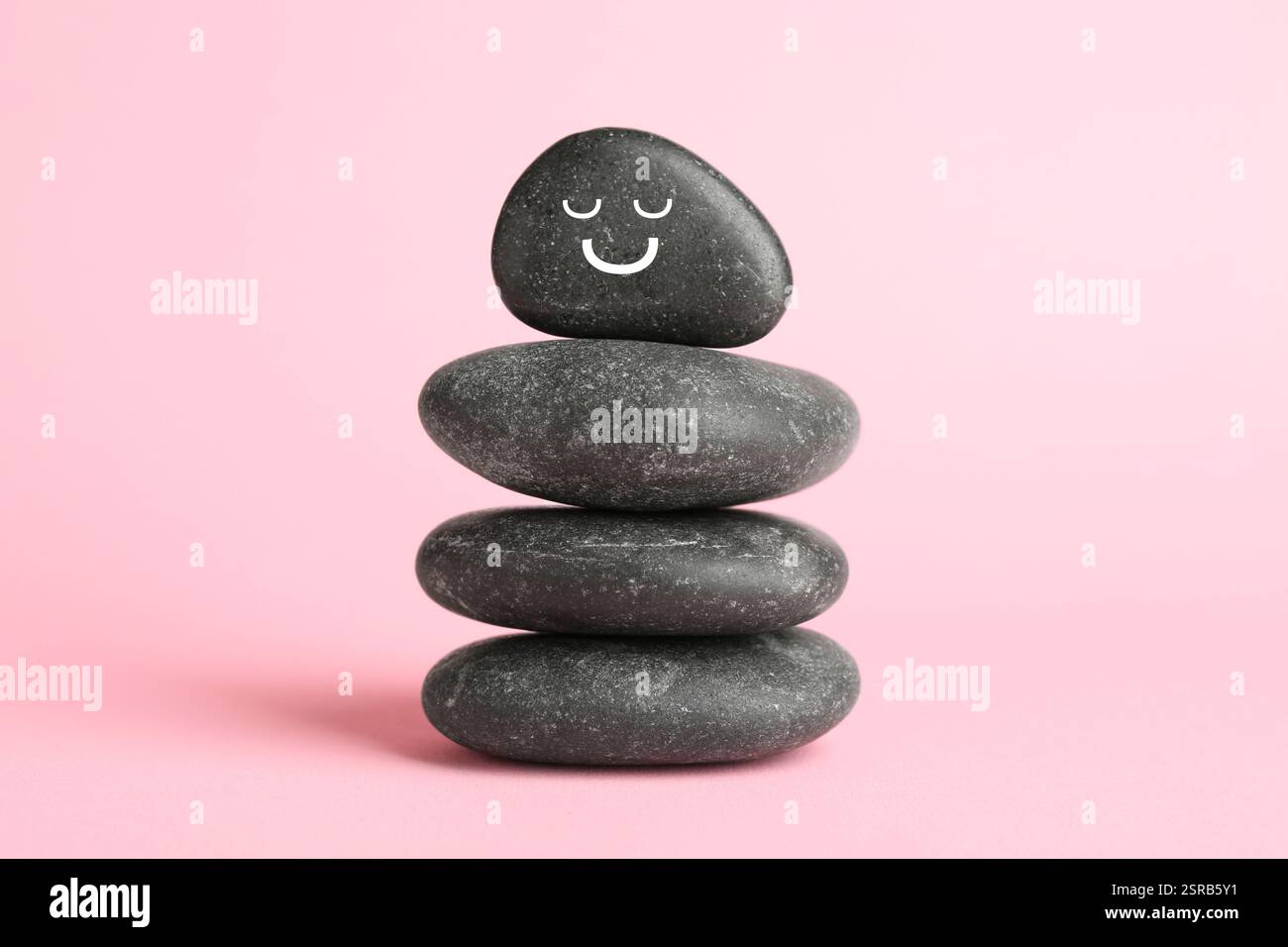 Stack of rocks with drawn smiley face on light pink background. Harmony ...