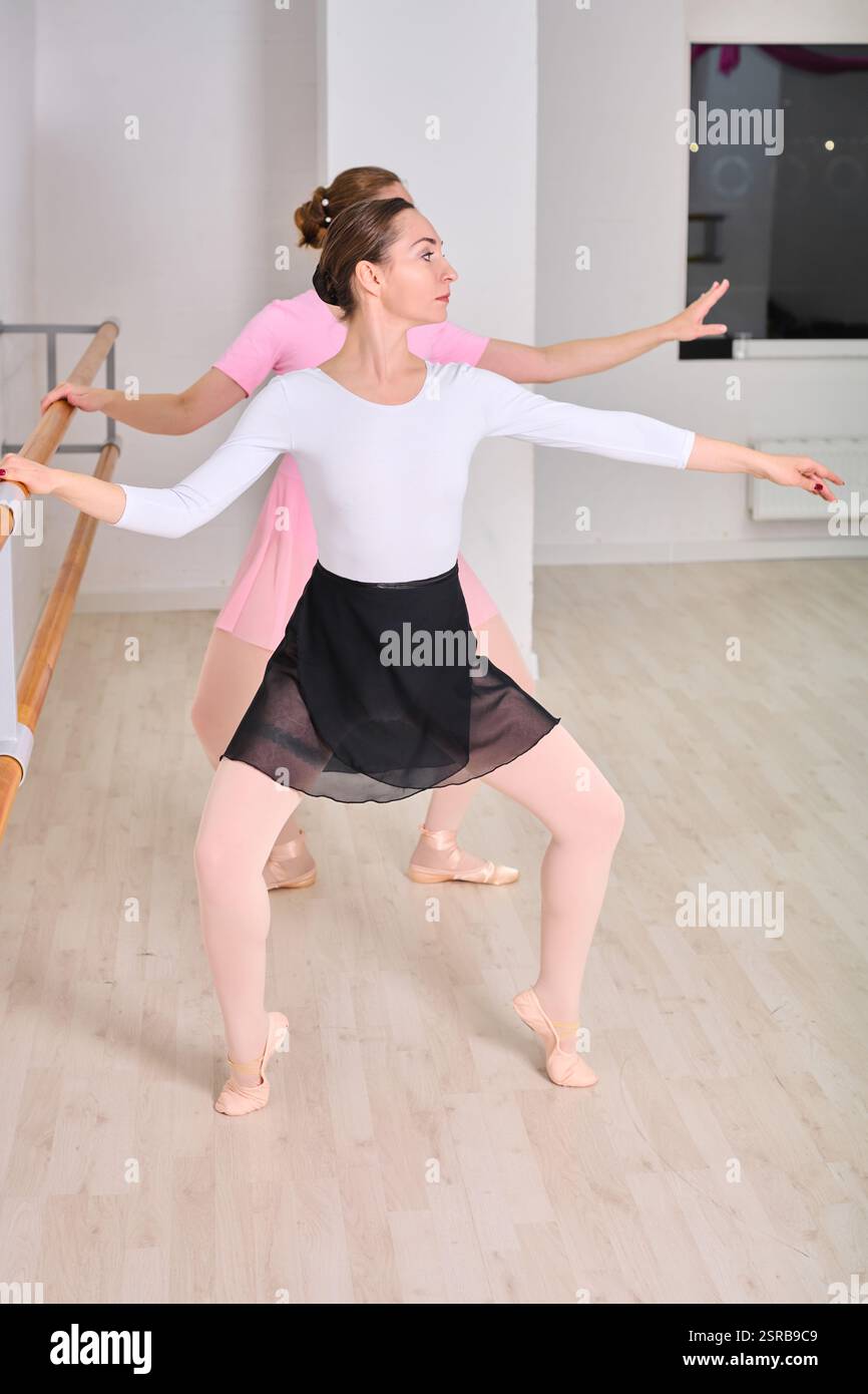 Two young female ballerinas with brown hair practicing ballet at barre ...