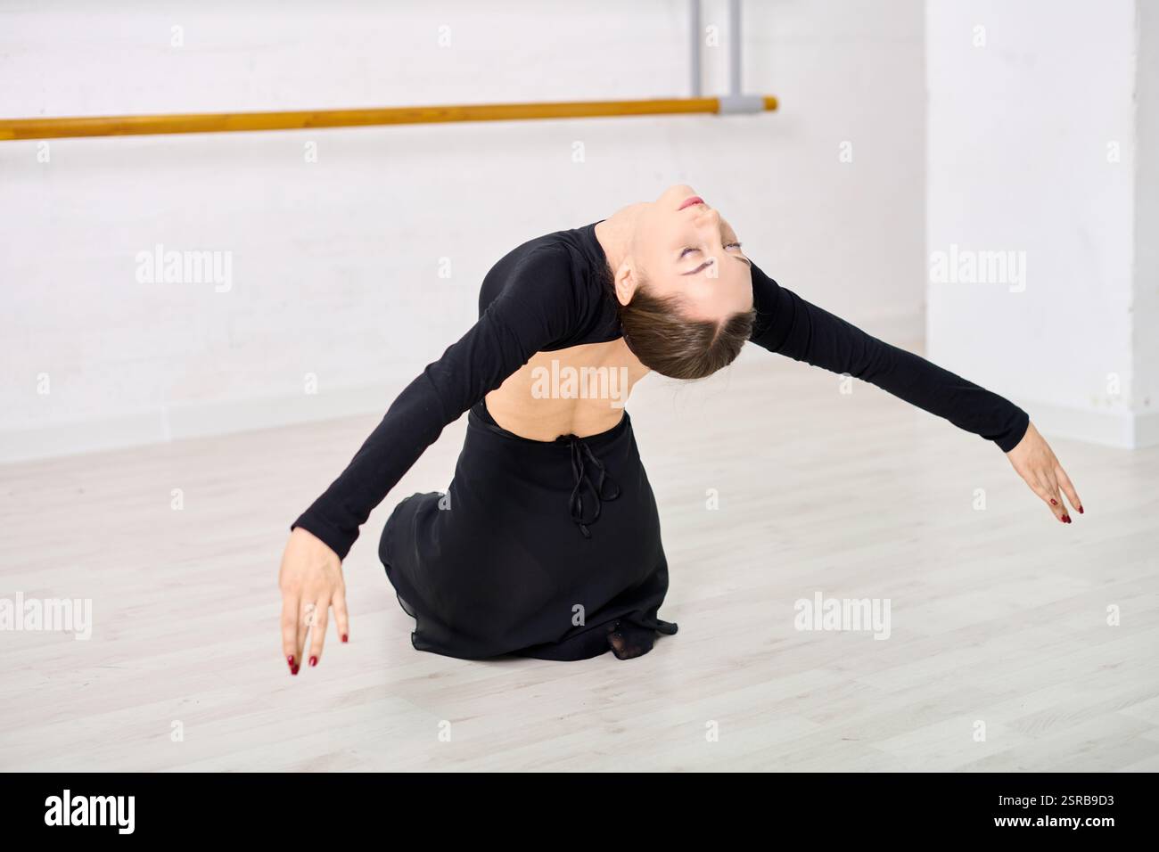Young female ballerina with brown hair kneels on studio floor, arching ...