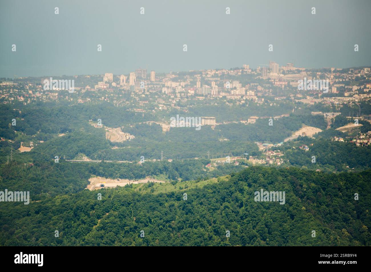 Cityscape viewed from high angle, surrounded by verdant hills. Soft ...