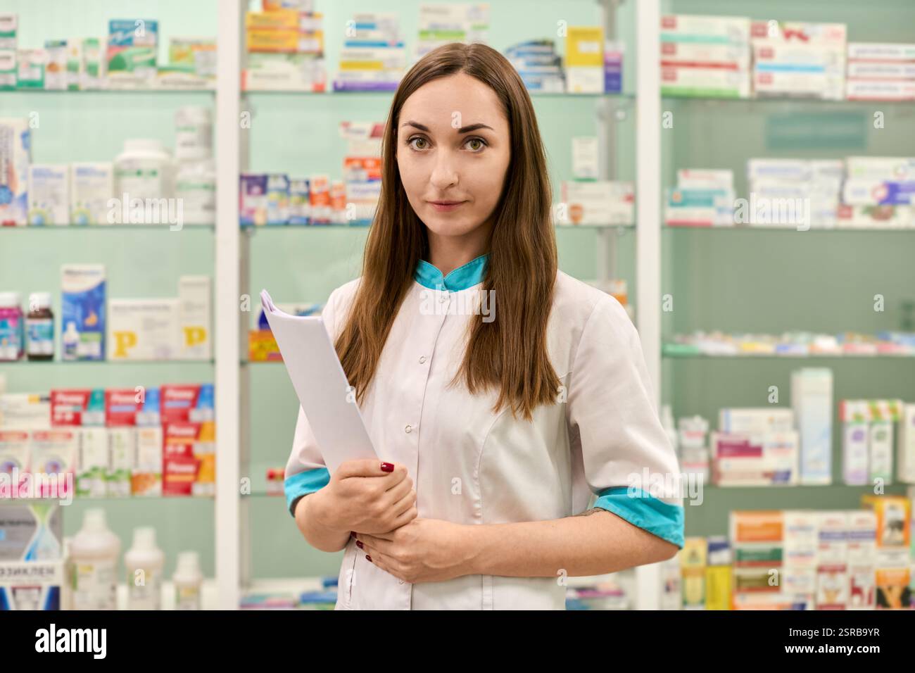 Young female pharmacist with long brown hair standing confidently in ...