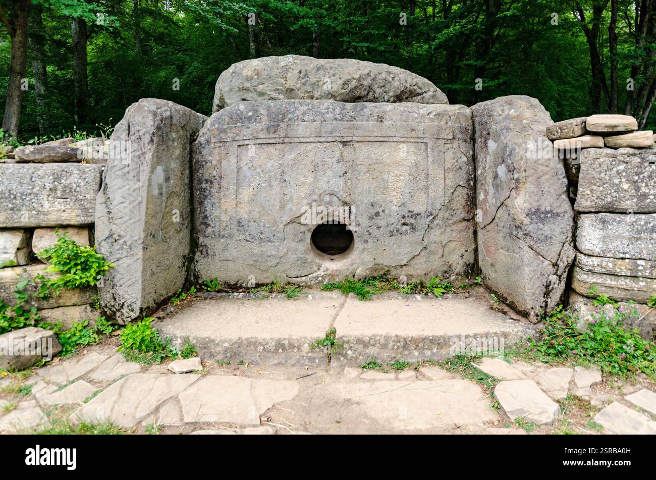 Stone dolmen with circular opening, surrounded by lush forest. Large ...