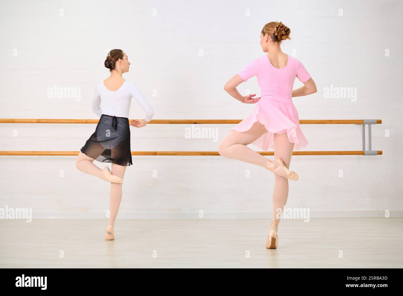 Young female ballerinas with light hair practicing at barre in bright ...