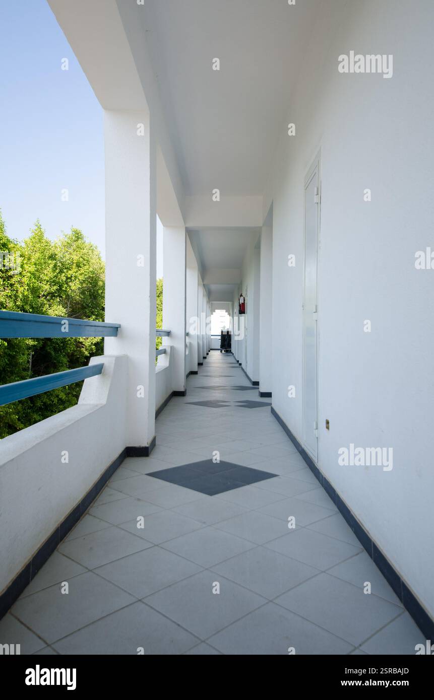 Long hotel corridor with white walls and tiled floor under bright ...