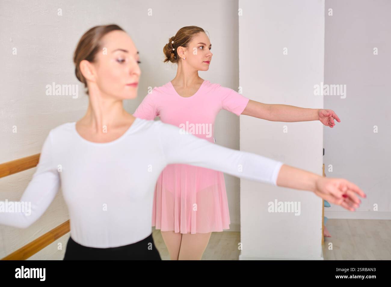 Two young adult female ballerinas practice at ballet barre. One with ...
