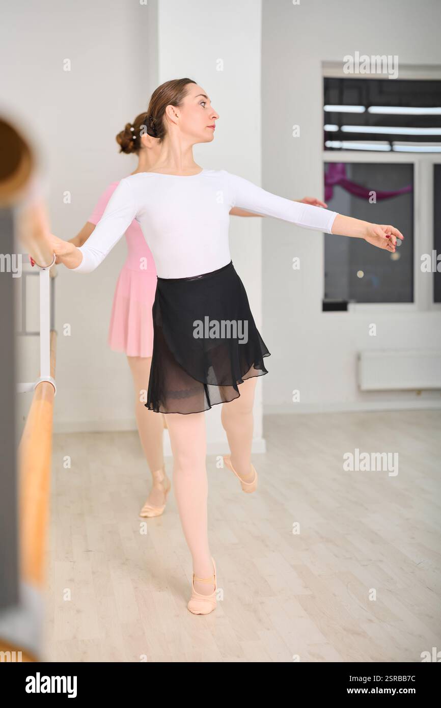 Two young female ballerinas practice at ballet barre in bright studio ...
