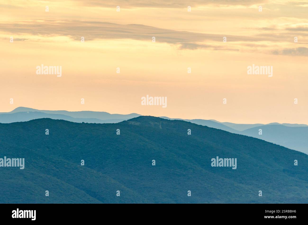 Layered mountain ridges under soft, golden dusk light create serene ...