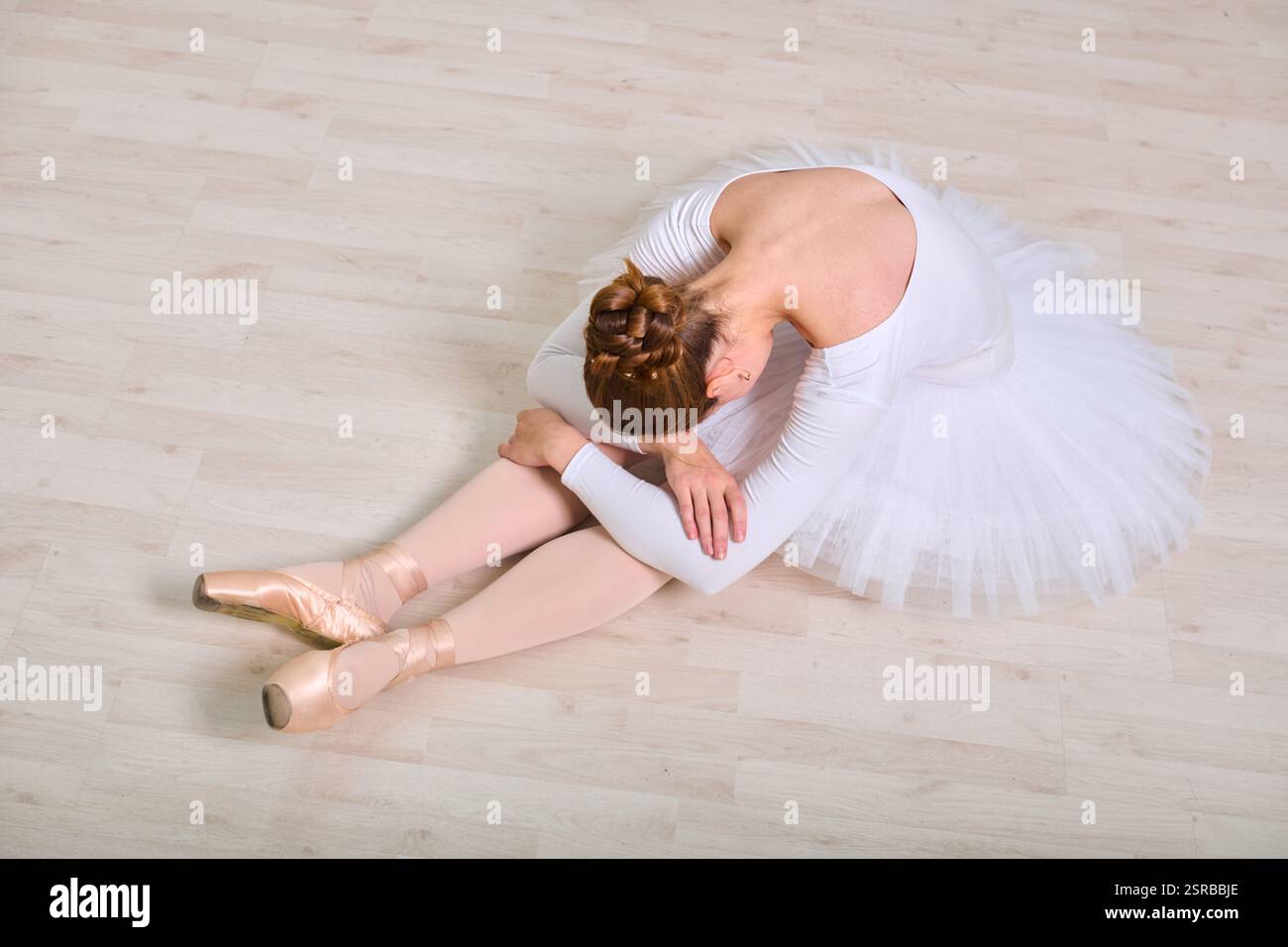 Young female ballerina with auburn hair in white tutu sits on light ...