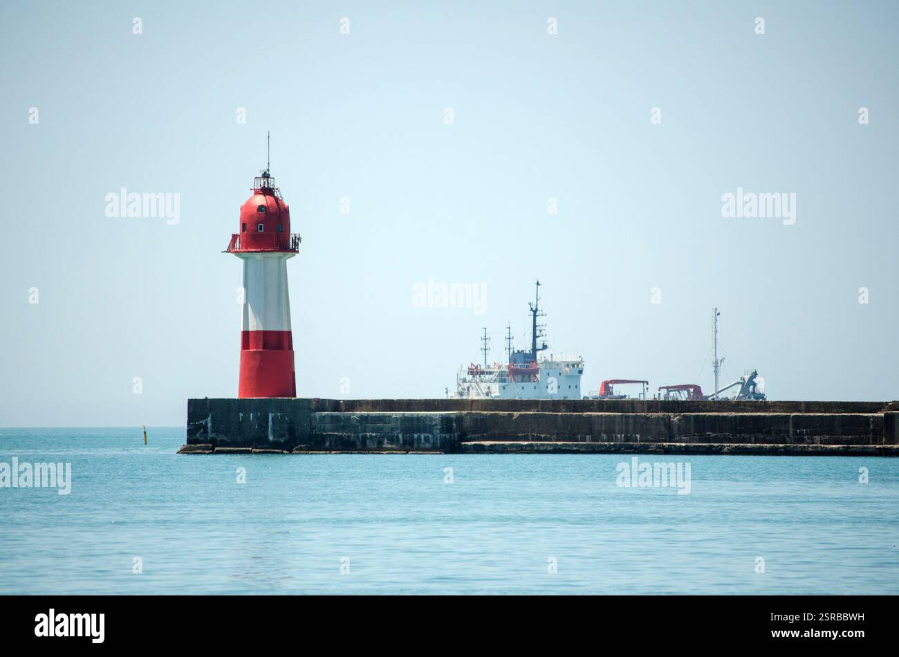 Red lighthouse stands on pier under clear sky, overlooking calm sea ...