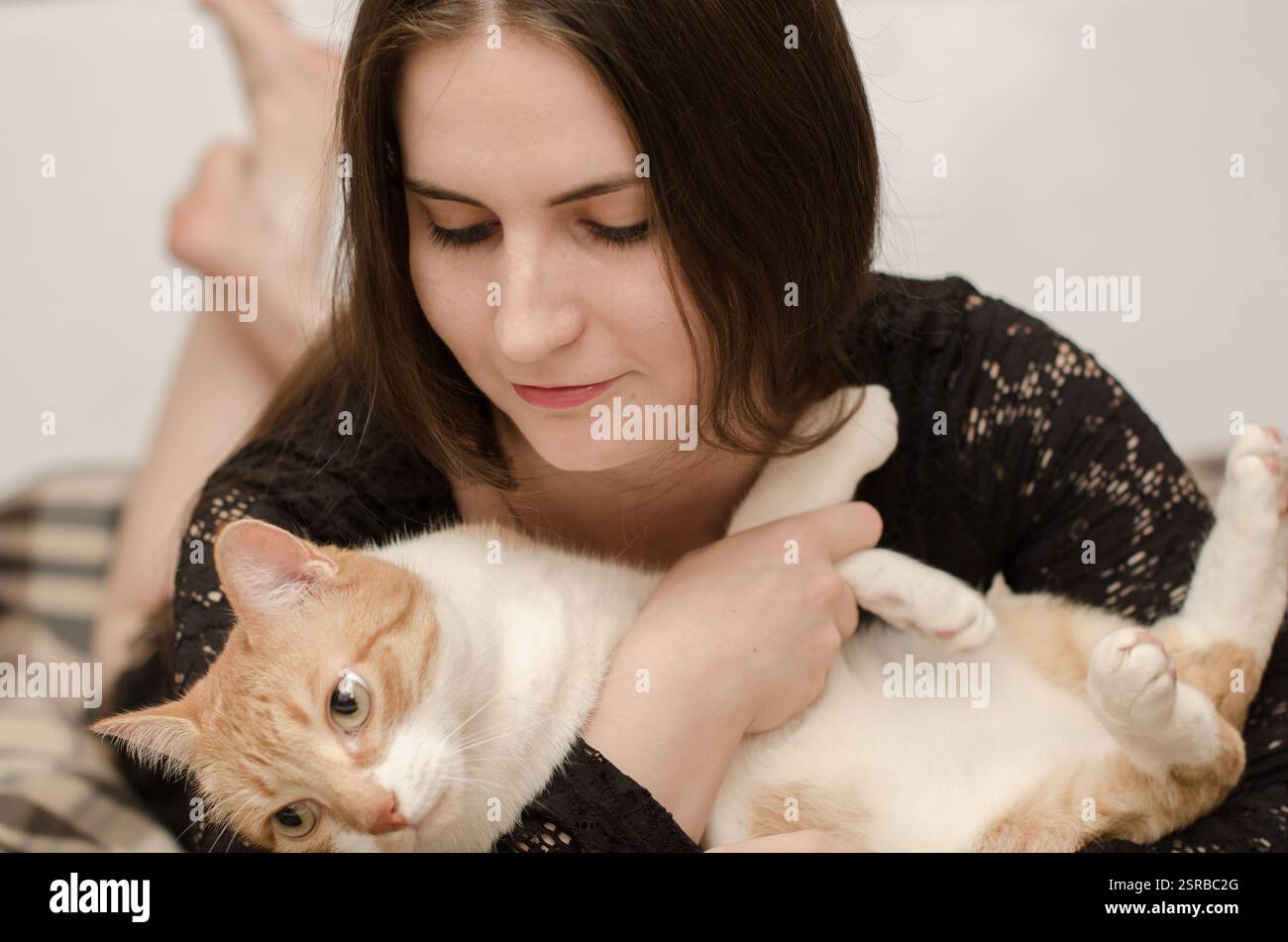 Young woman with long brown hair lovingly cradles ginger cat. Indoors ...