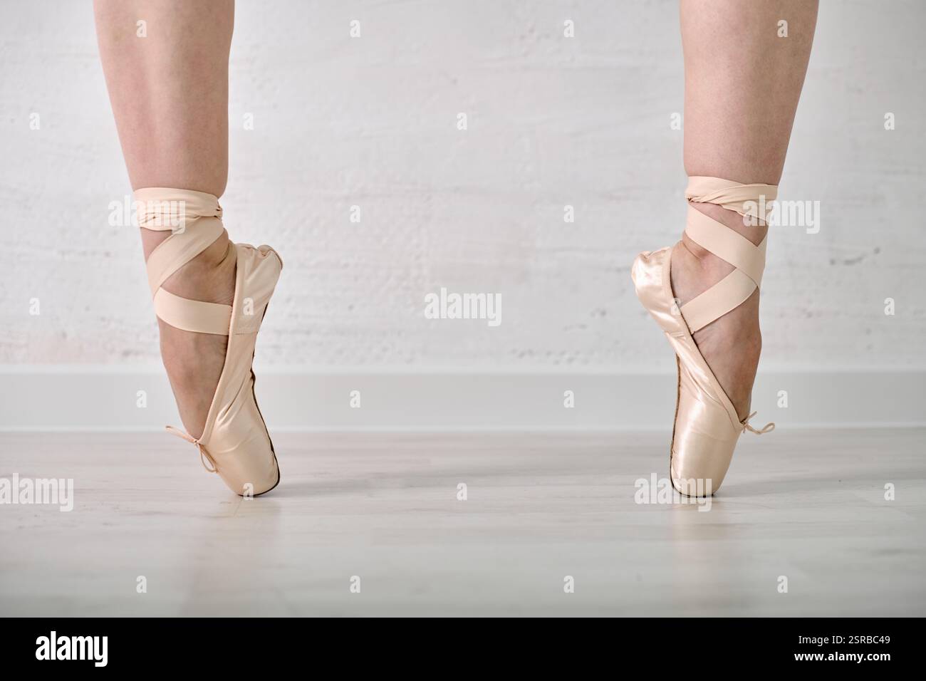 Close-up of young female ballet dancers feet in pointe shoes against minimal white wall. Soft ...