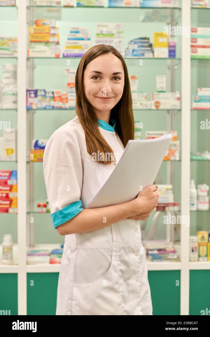 Young female pharmacist with long brown hair and smile stands ...