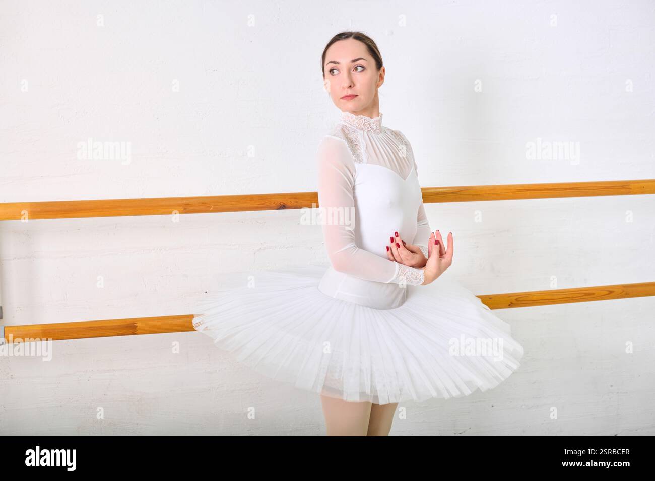 Young adult female ballerina with brown hair in white tutu poses ...