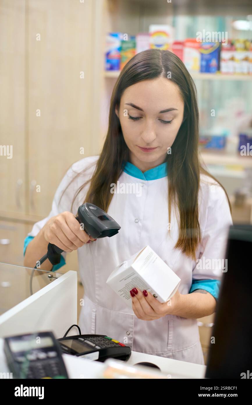 Young female pharmacist with brown hair scans medication package at ...