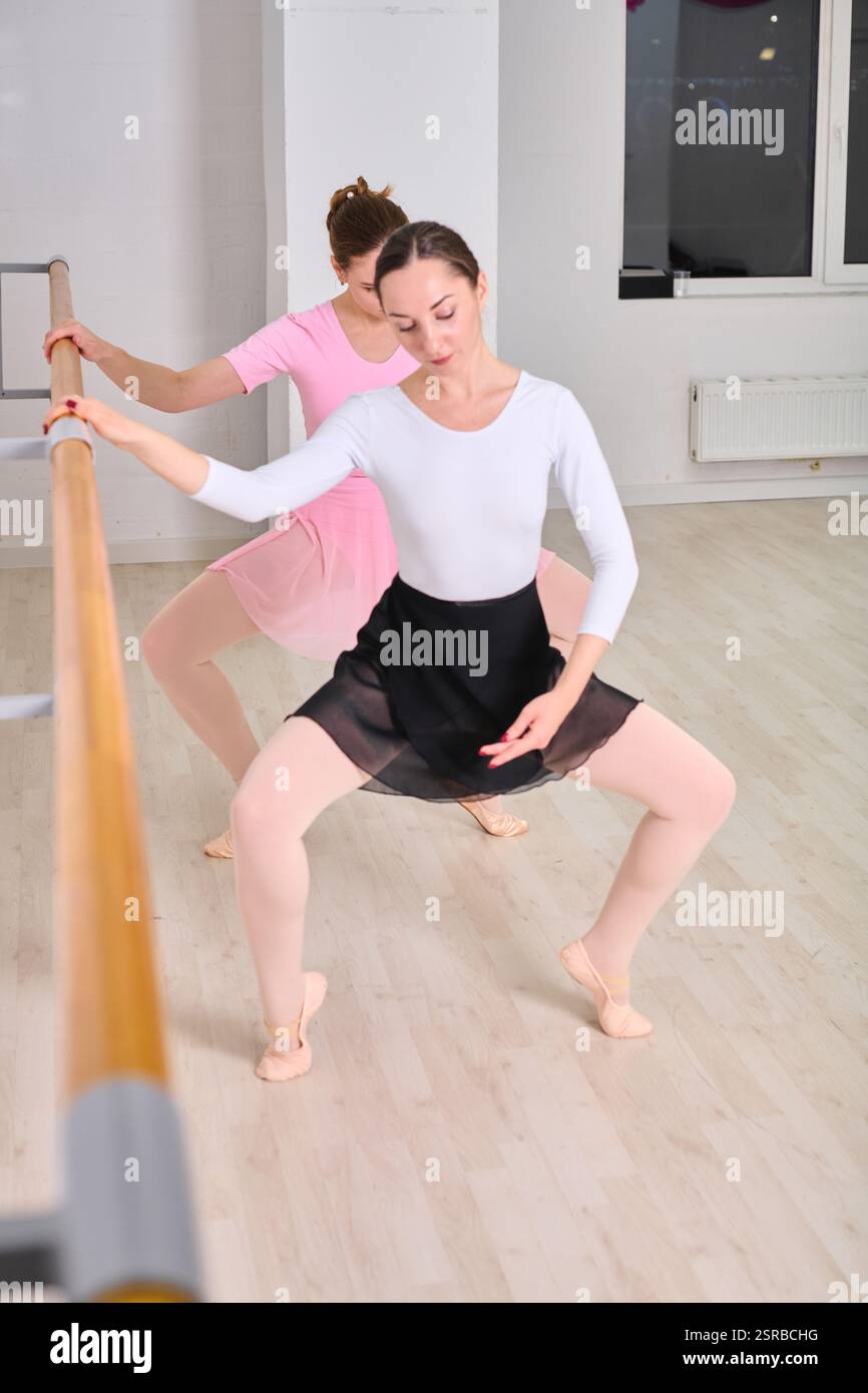 Two young female ballerinas with brown hair practicing ballet at barre ...
