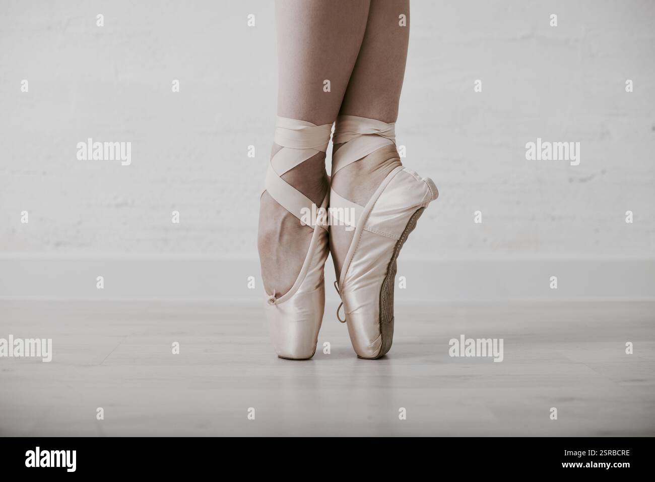 Close-up of young ballerinas feet on wooden floor. Light skin and delicate pointe shoes create ...