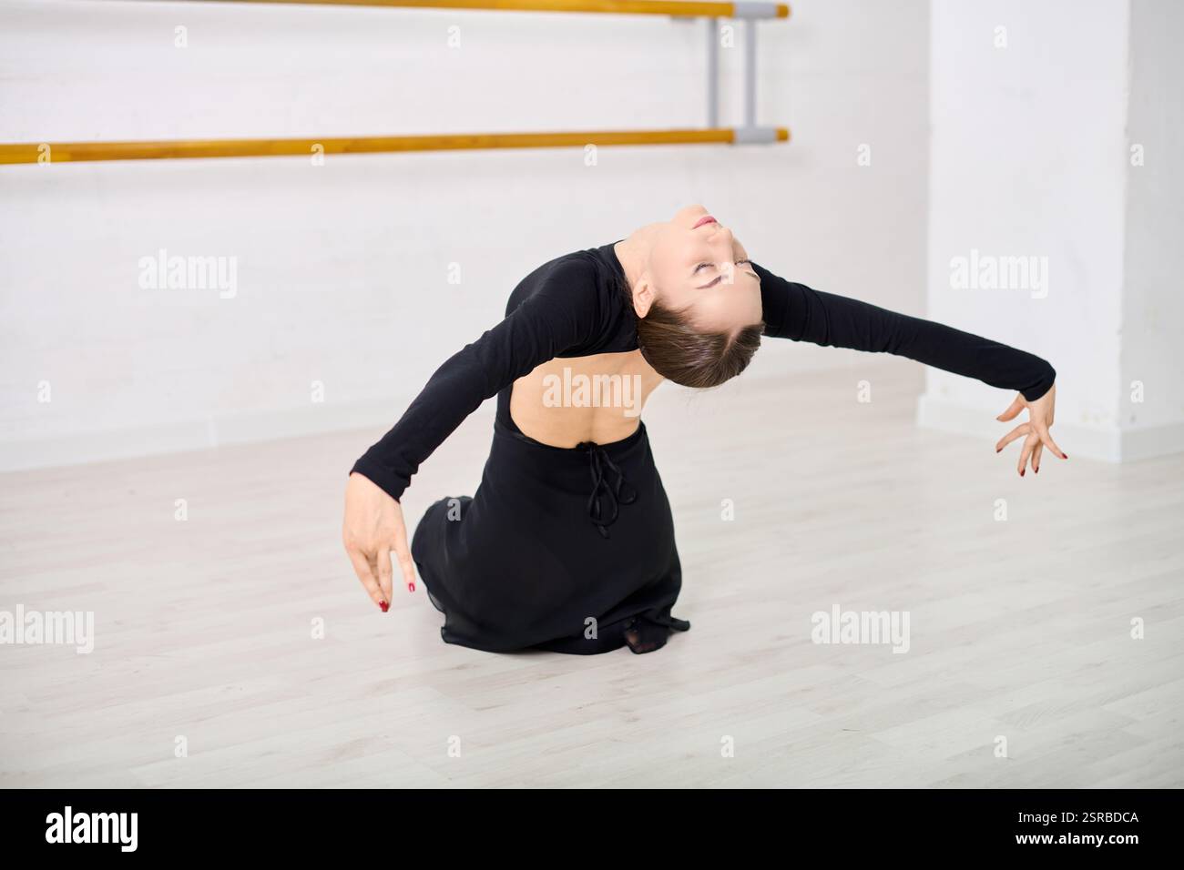 Young female ballerina with brown hair kneels on studio floor, arching ...