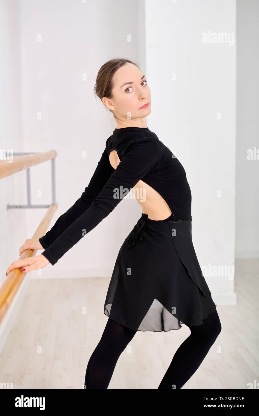Young adult female ballerina with brown hair in black attire strikes ...