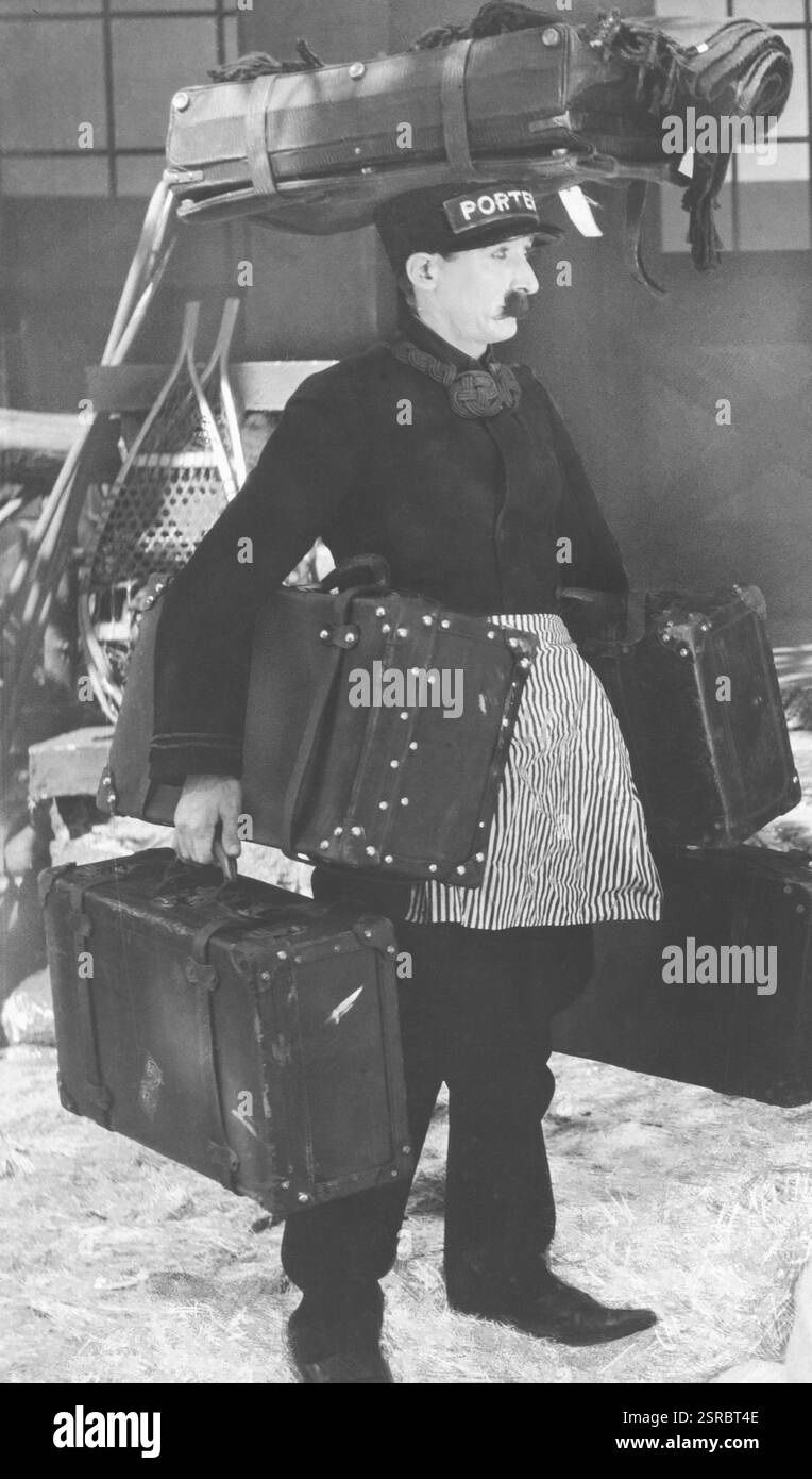 Old time photo of a male Porter carrying luggage in both hands and one ...