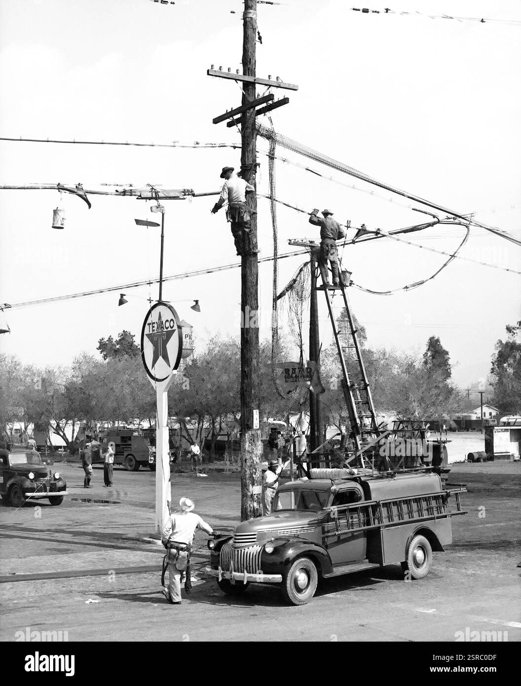 Several men on a line crew working off a telephone pole and ladders off ...