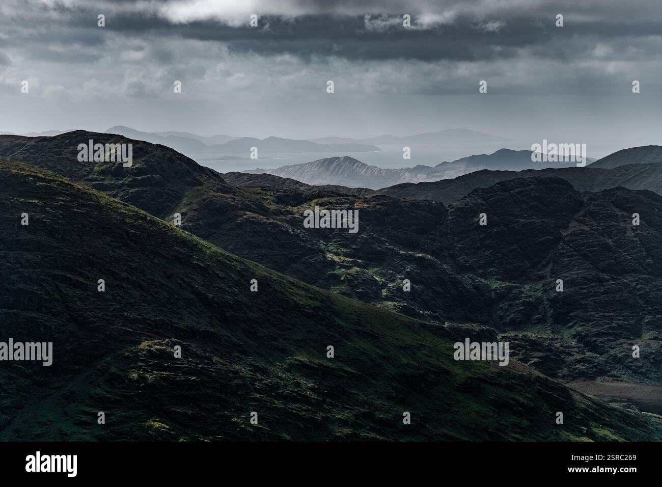 A landscape photograph showing several dark mountain ranges. The ...