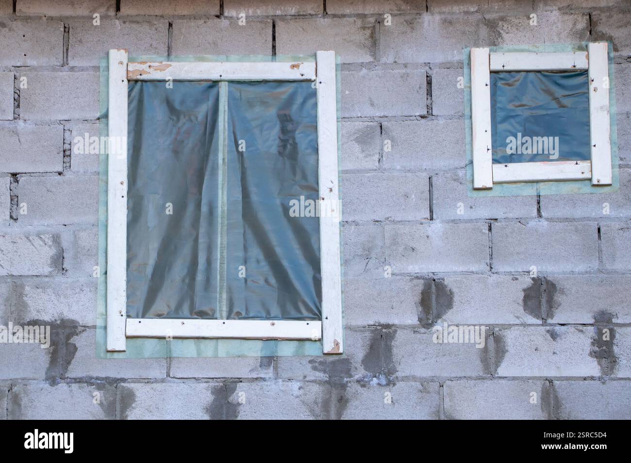 two windows on the side wall of an old concrete house with plastic ...
