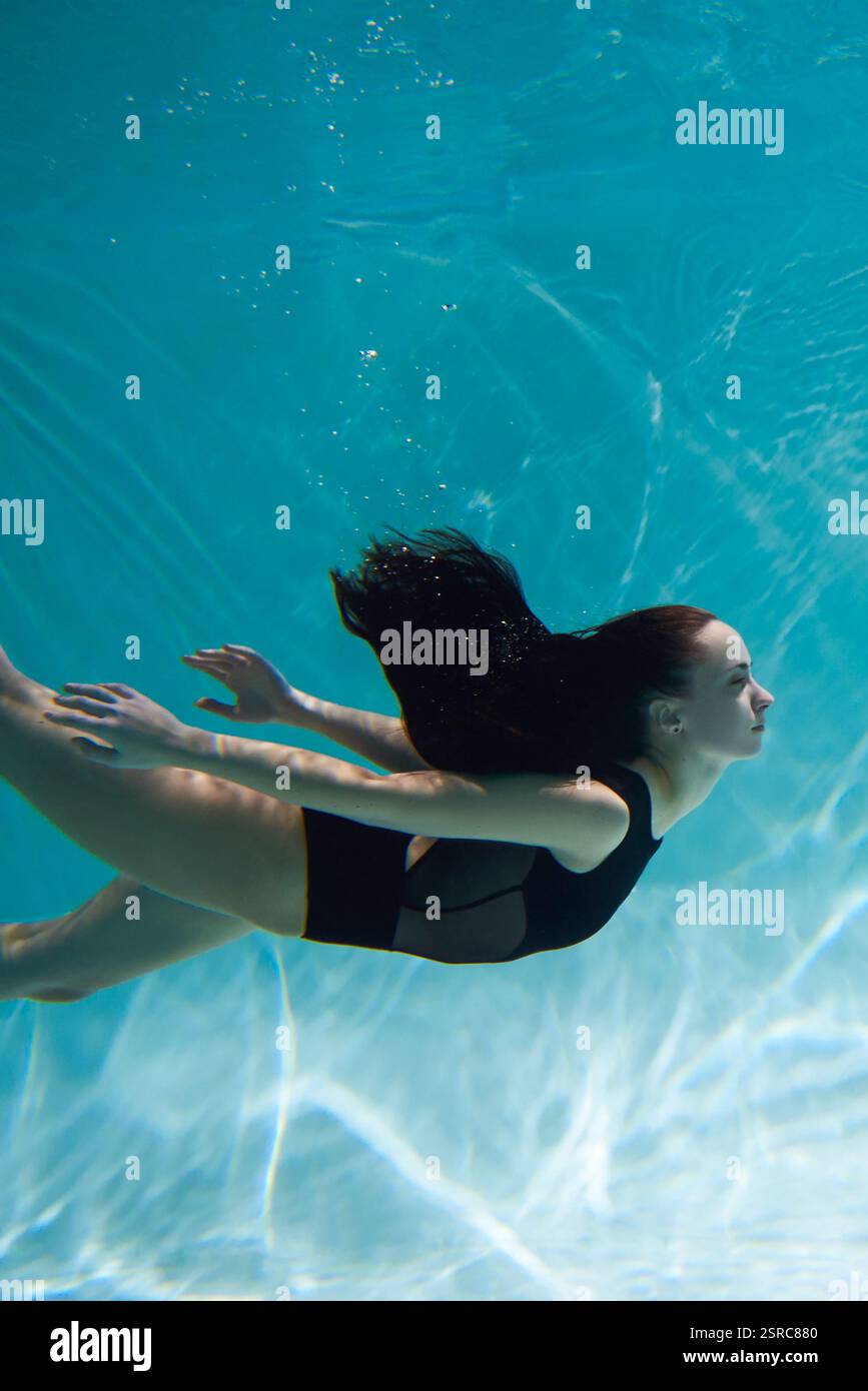 Underwater portrait of a female model in a black swimsuit. She floats ...
