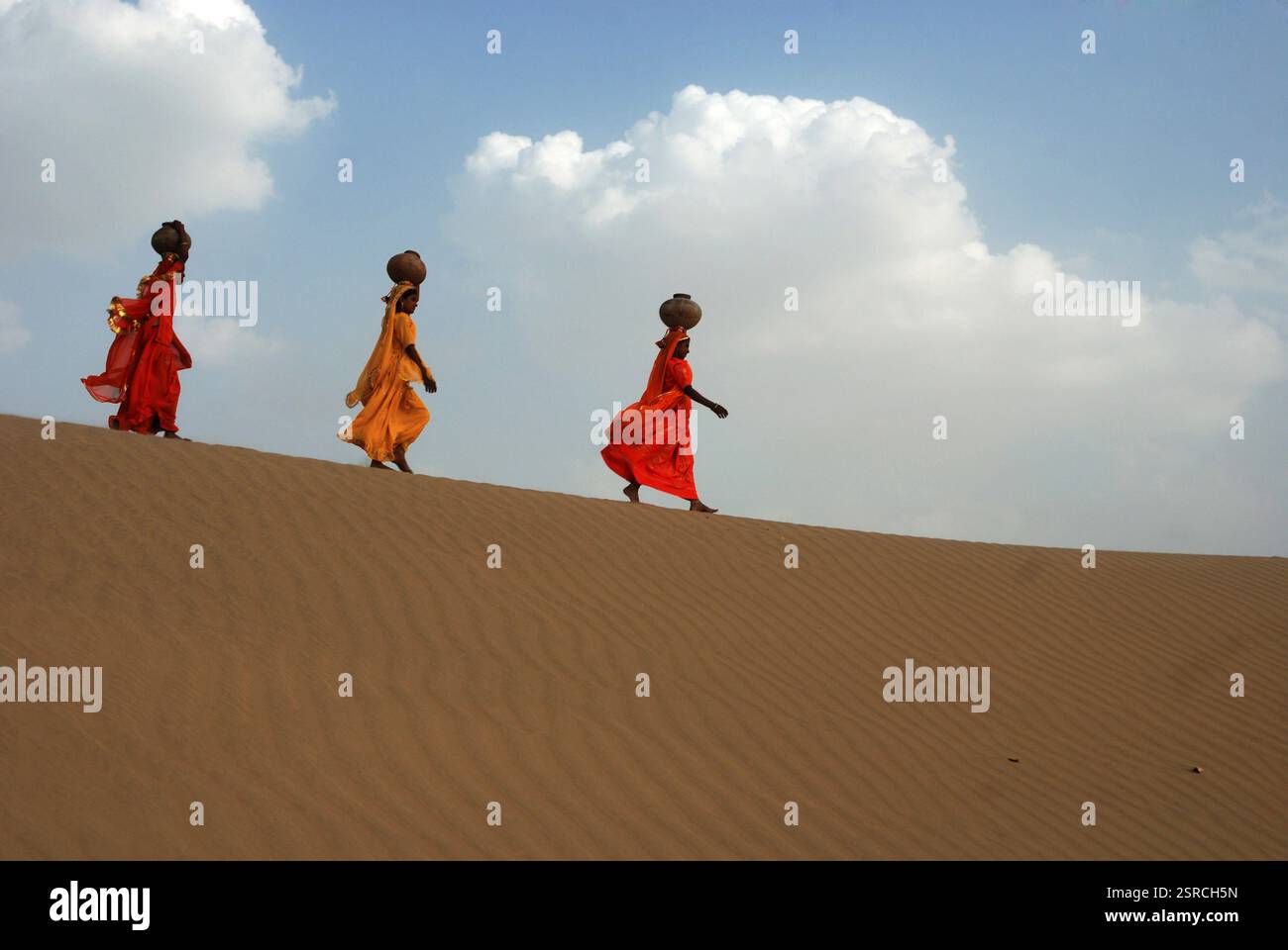 Rajasthani women with pitchers on head walking down on sand dune of ...