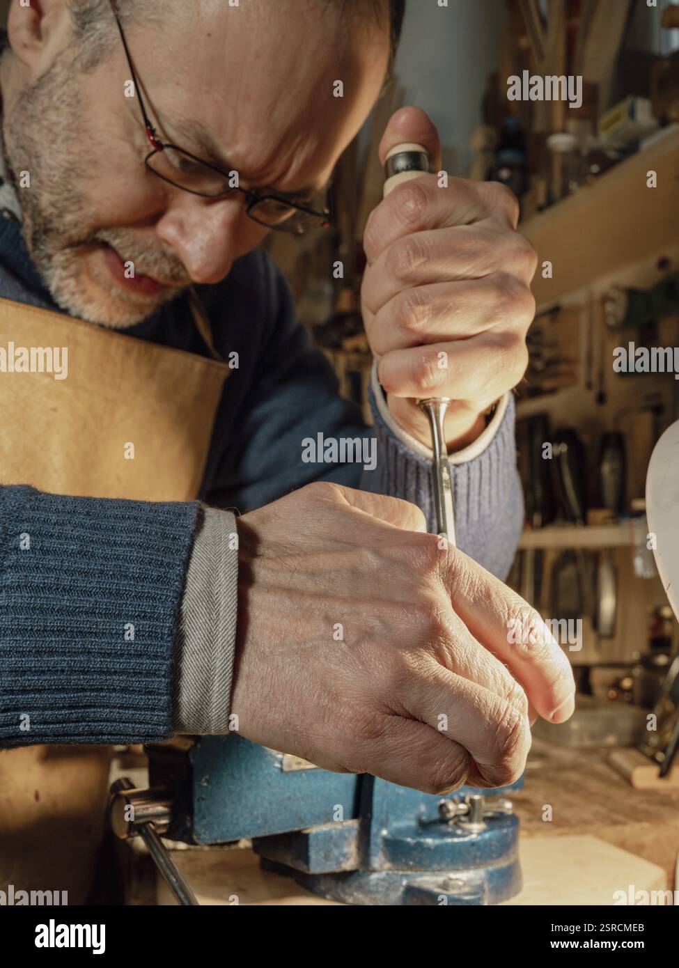 Artisan luthier carefully carving a piece of wood secured in a vise ...