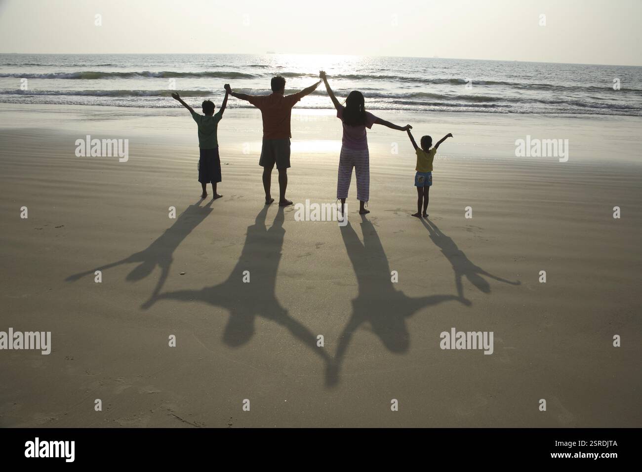 South Asian Indian parent and children holding hands facing sun with ...
