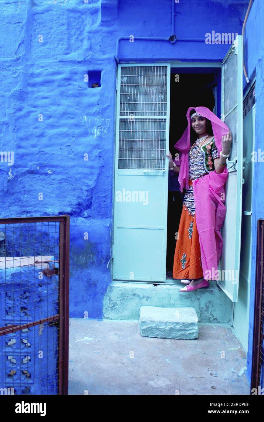 Girl in pink odhani standing on the door of blue house in brahmapuri, Jodhpur, Rajasthan, India ...