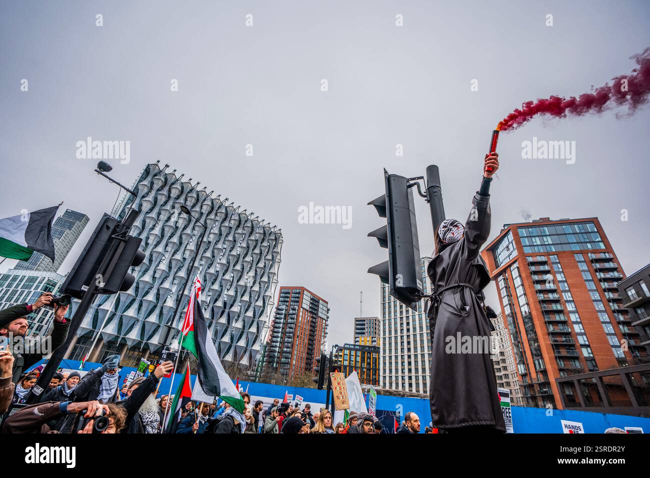 London, UK. 15th Feb, 2025. A masked protestor lights a blood-red flare ...